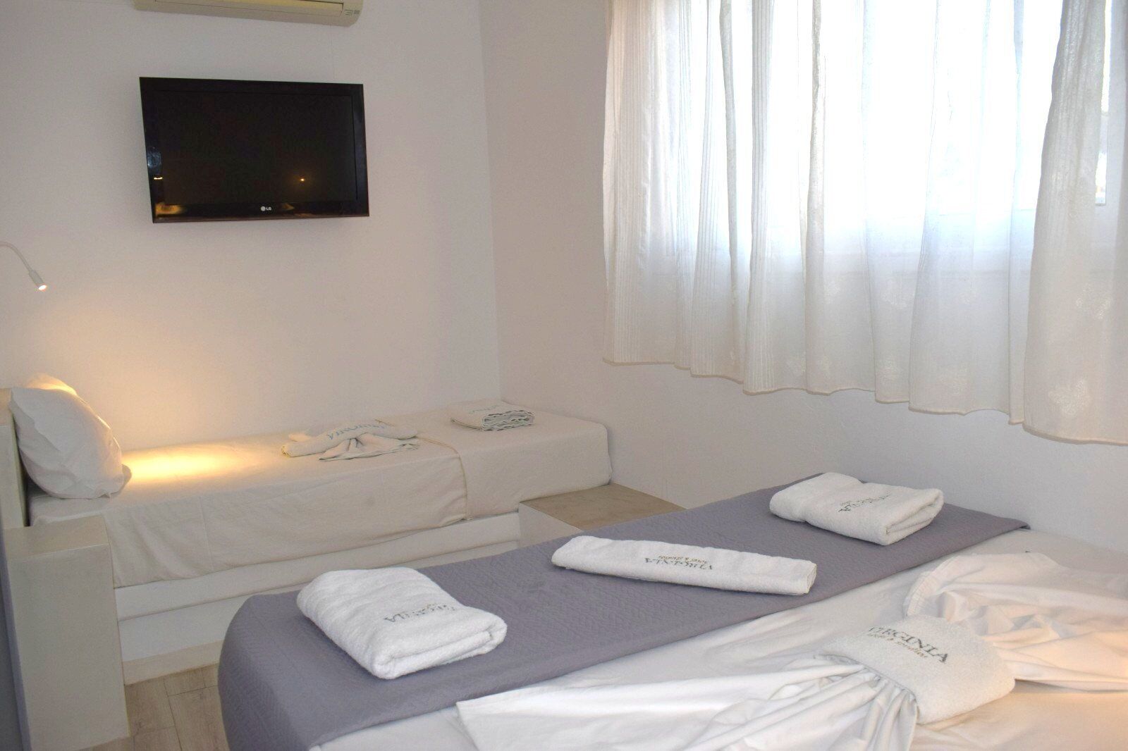 Quarto de hotel com cama, sofá, televisão e janela com cortinas.