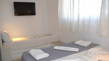 Quarto de hotel com cama, sofá, televisão e janela com cortinas.