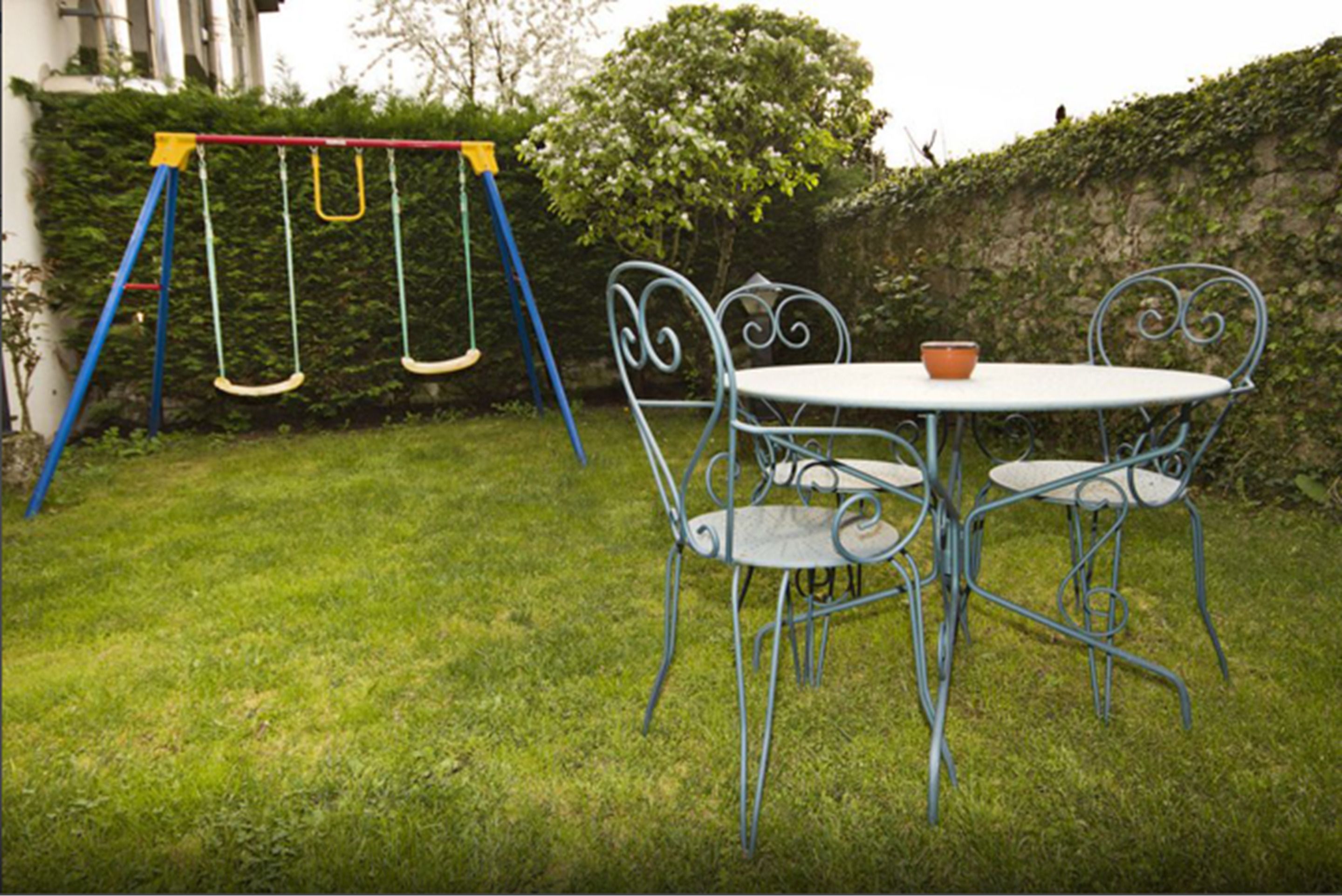 Um jardim com balanço e uma mesa redonda com cadeiras.