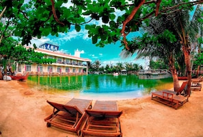 Um hotel à beira-mar com piscina, espreguiçadeiras e um edifício com varandas com vista para o mar.