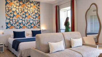 Quarto de hotel com cama, sofá, um espelho grande e um design floral na parede.