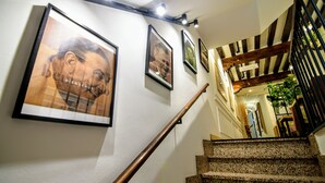Uma escadaria com corrimão de madeira e degraus de granito, levando a um patamar com quadros nas paredes.