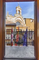 Vista pela janela de um edifício com fachada de pedra, telhado de telhas e um campanário.