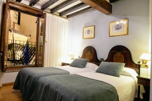 Quarto de hotel com duas camas, cabeceira de madeira, janela com vista para uma escadaria e quadros nas paredes.