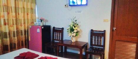 Quarto de hotel com uma cama, televisão na parede, uma mesinha com um vaso de flores, duas cadeiras e uma porta.