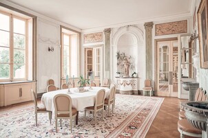Uma sala de jantar ampla com uma mesa redonda grande, várias cadeiras e um tapete decorativo.