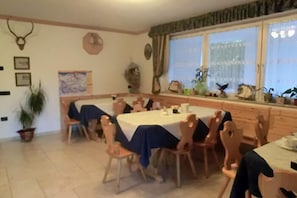 Uma área de refeições com uma grande mesa redonda coberta por um pano de mesa azul, cercada por cadeiras de madeira.