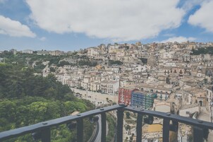 Uma cidade histórica situada numa encosta íngreme, com edifícios antigos e um prédio vermelho de destaque, e uma estrada descendo.
