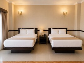 Quarto de hotel com duas camas, uma mesa de cabeceira com luminária e arandelas na parede.