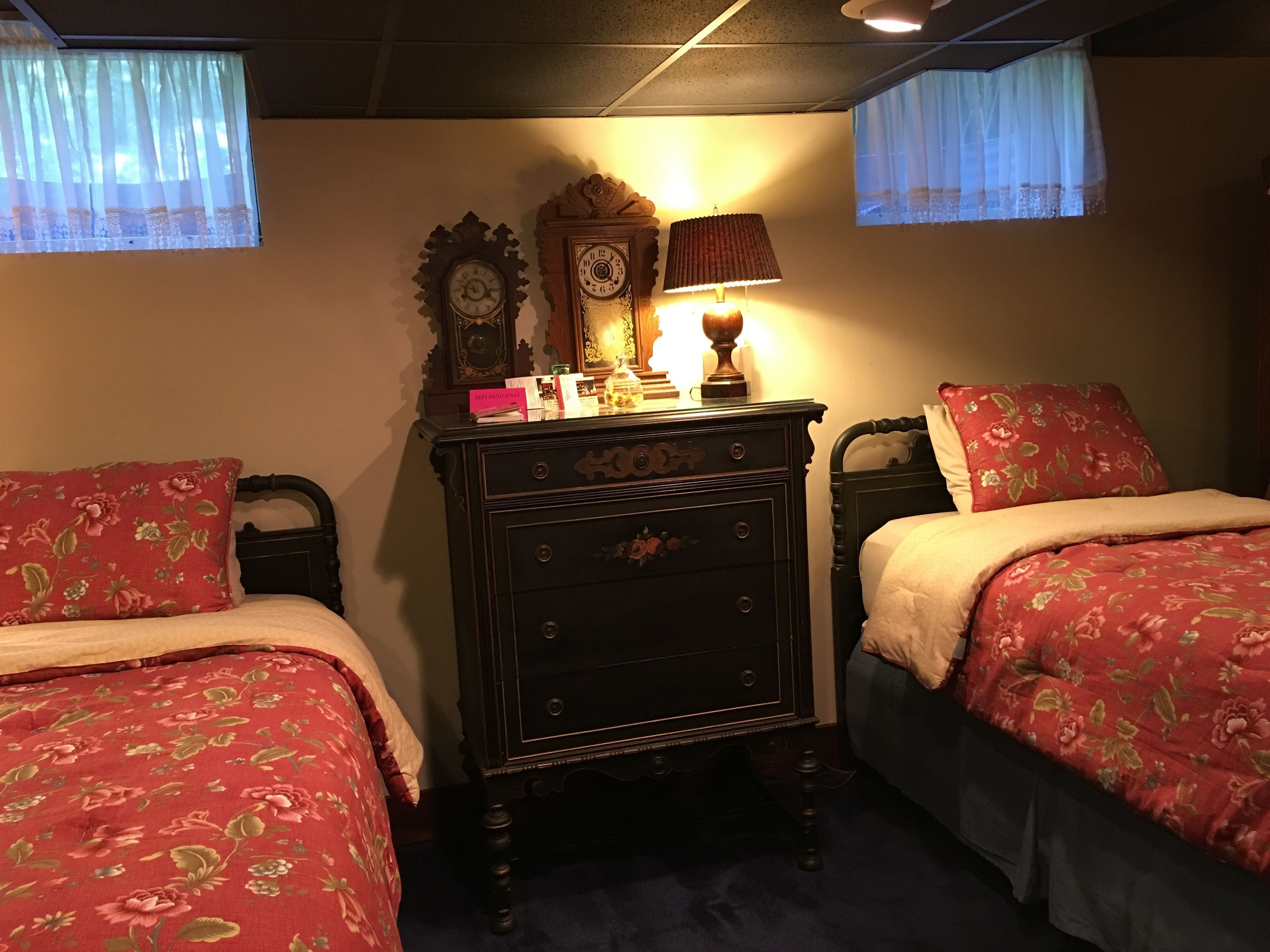 Quarto com duas camas, uma cômoda, um relógio e um abajur.