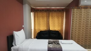 Quarto de hotel com duas camas, uma poltrona de couro preto e uma janela com cortinas.