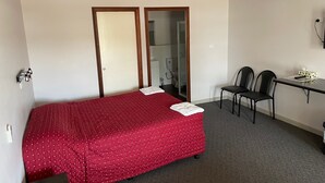 Um quarto pequeno e bem organizado, com uma cama de solteiro, uma escrivaninha, duas cadeiras e um espelho.