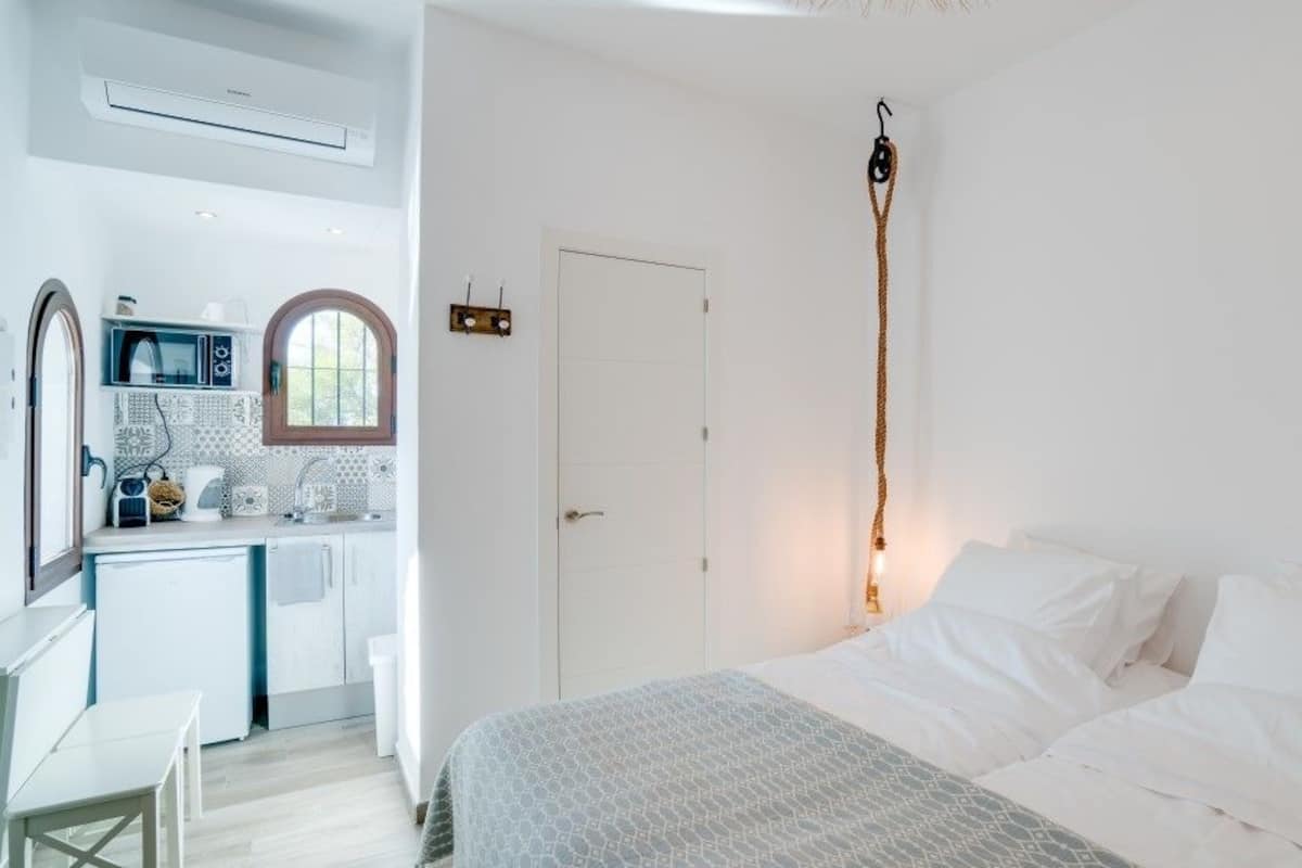 Quarto com cama, mesa de cabeceira e luminária suspensa.