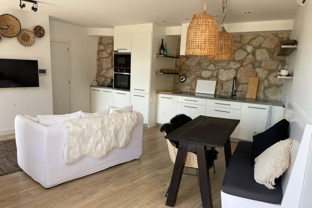 Uma sala de estar moderna com um sofá branco, uma mesa de jantar preta e uma parede de destaque em pedra.