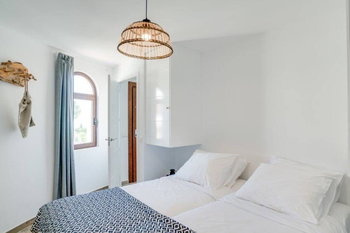 Quarto com uma cama, luminária pendente e porta que dá para outro cômodo.
