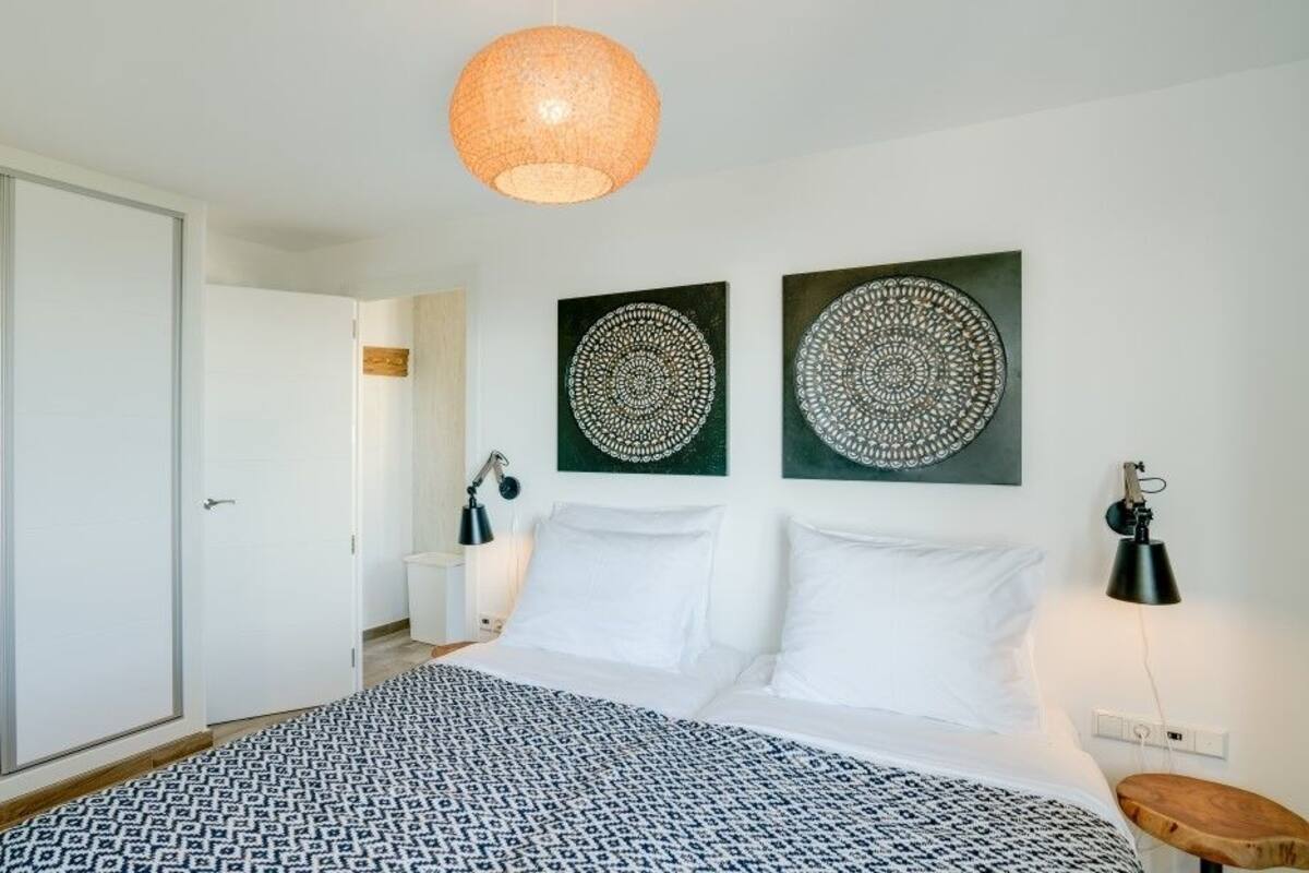 Quarto com uma cama, duas luminárias fixadas na parede e duas obras de arte circulares.