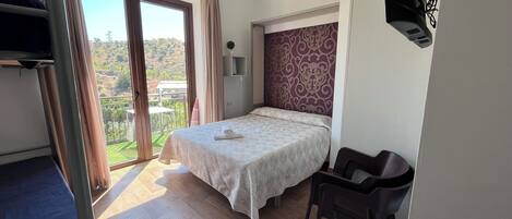 Quarto com cama beliche, uma cama de solteiro, uma cadeira e vista para uma paisagem verde pela janela.