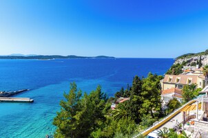 Vista costeira com águas azul-claras, um cais e edifícios com varandas viradas para o mar.