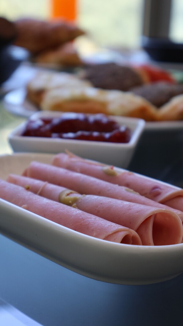 Uma mesa com diversos alimentos, incluindo enroladinhos de fiambre, um recipiente com ketchup e um prato com vários pratos.