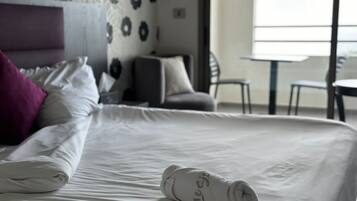 Cama bem arrumada com uma toalha enrolada e um travesseiro bordado com 'Le Site'.