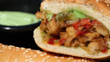 Sanduíche com ingredientes visíveis, como frango, vegetais e molho, acompanhado de um molho para acompanhar.