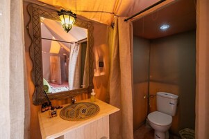 Um banheiro com toucador de madeira, espelho decorativo, vaso sanitário e cortina de chuveiro.