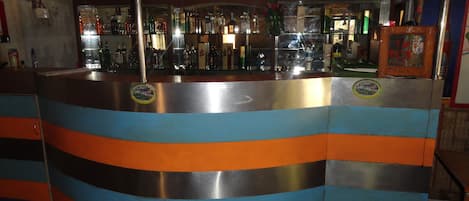 Uma área de bar com balcão, diversas garrafas e um aviso sobre cobrança e taxa de IVA.
