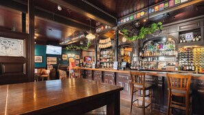 Um bar com móveis de madeira, um bartender e uma variedade de garrafas e copos.
