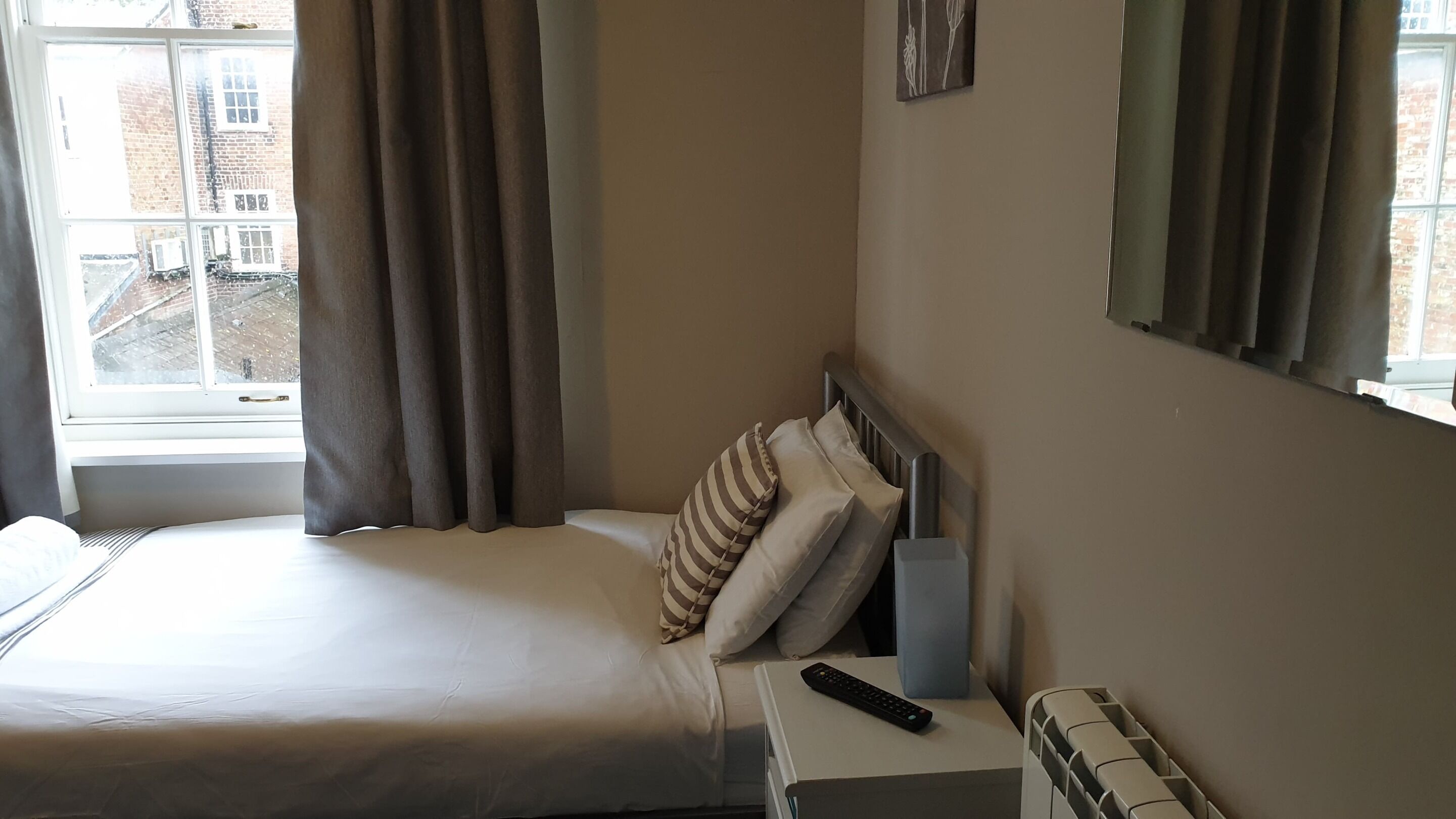 Quarto com cama, mesa de cabeceira e cortinas na janela.