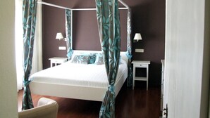 Uma cama de dossel com cortinas, duas mesas de cabeceira e uma cadeira.