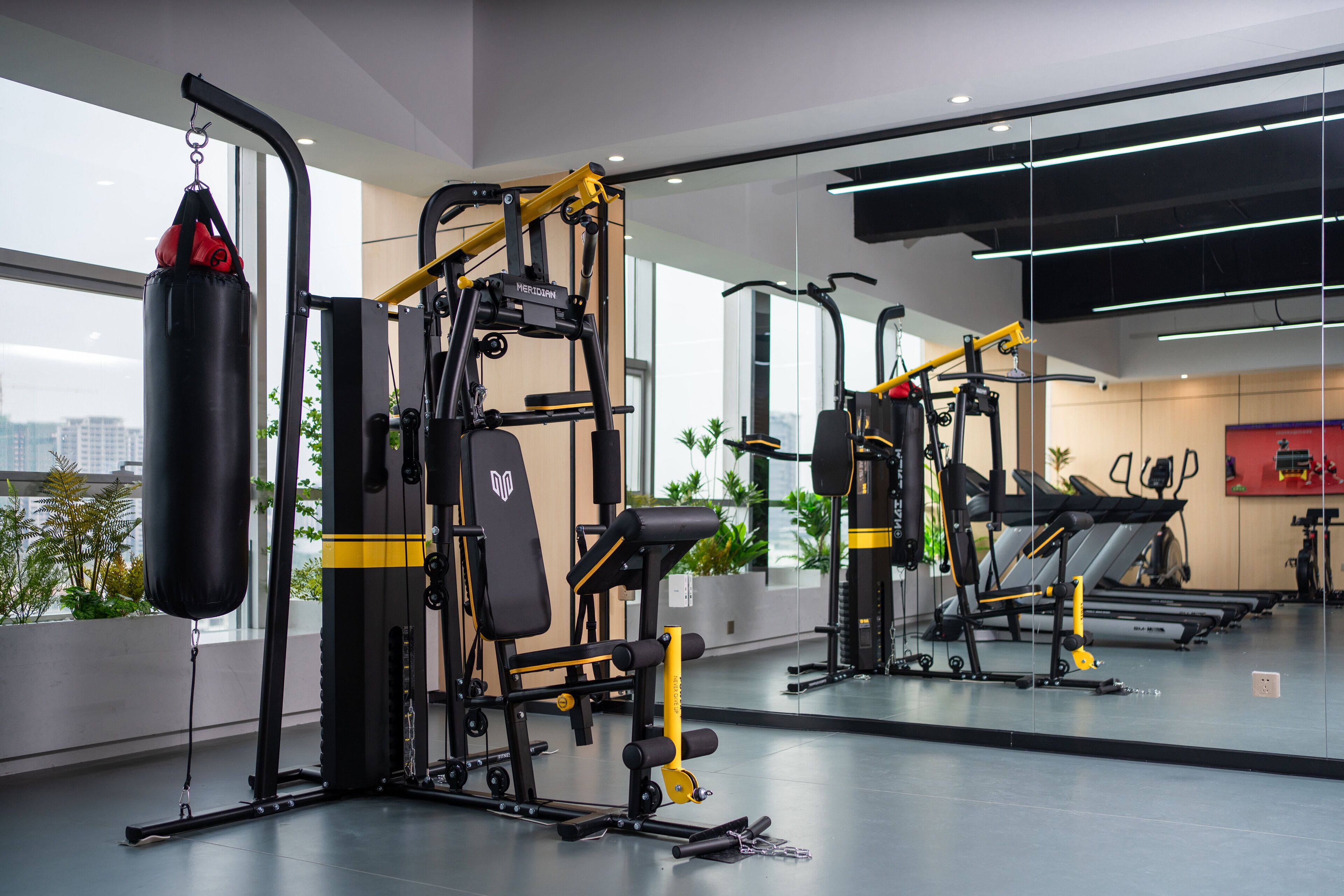 Uma academia com equipamentos de ginástica, um saco de pancadas e um espelho grande refletindo o espaço.
