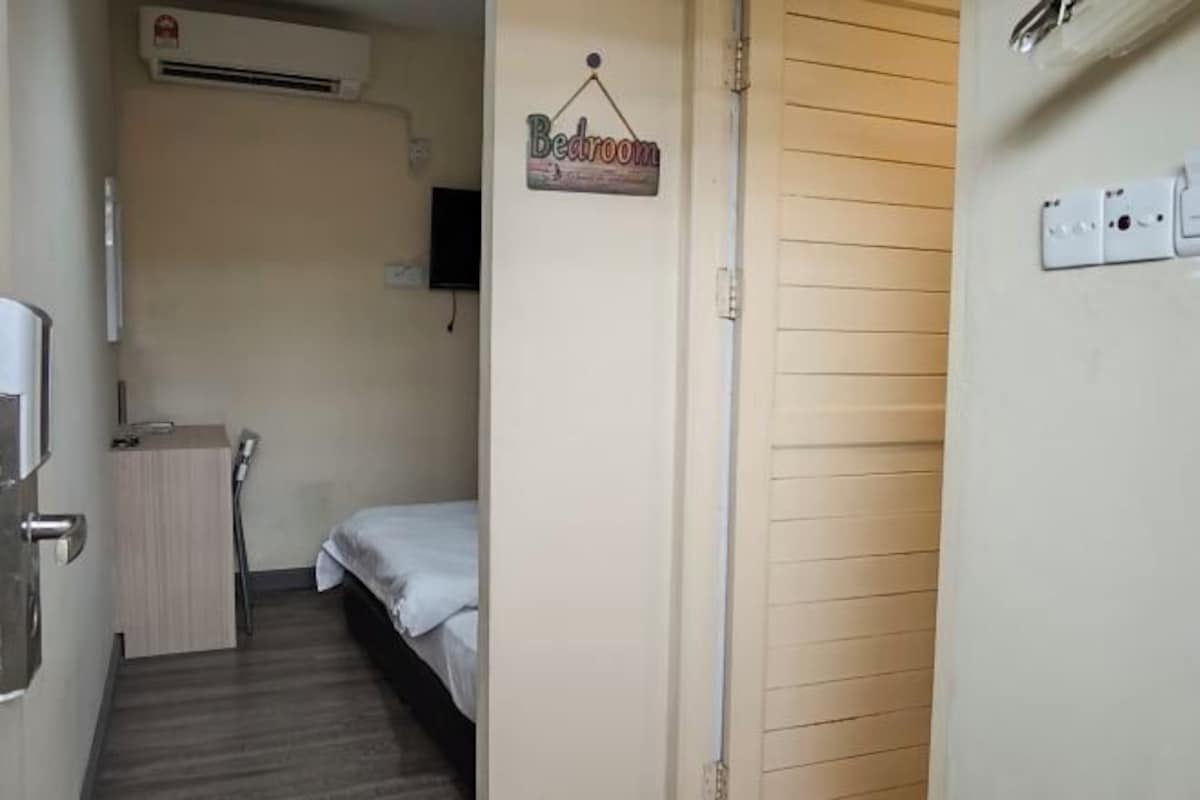 Quarto com cama, mesa de cabeceira, TV fixada na parede e placa indicativa do aposento.