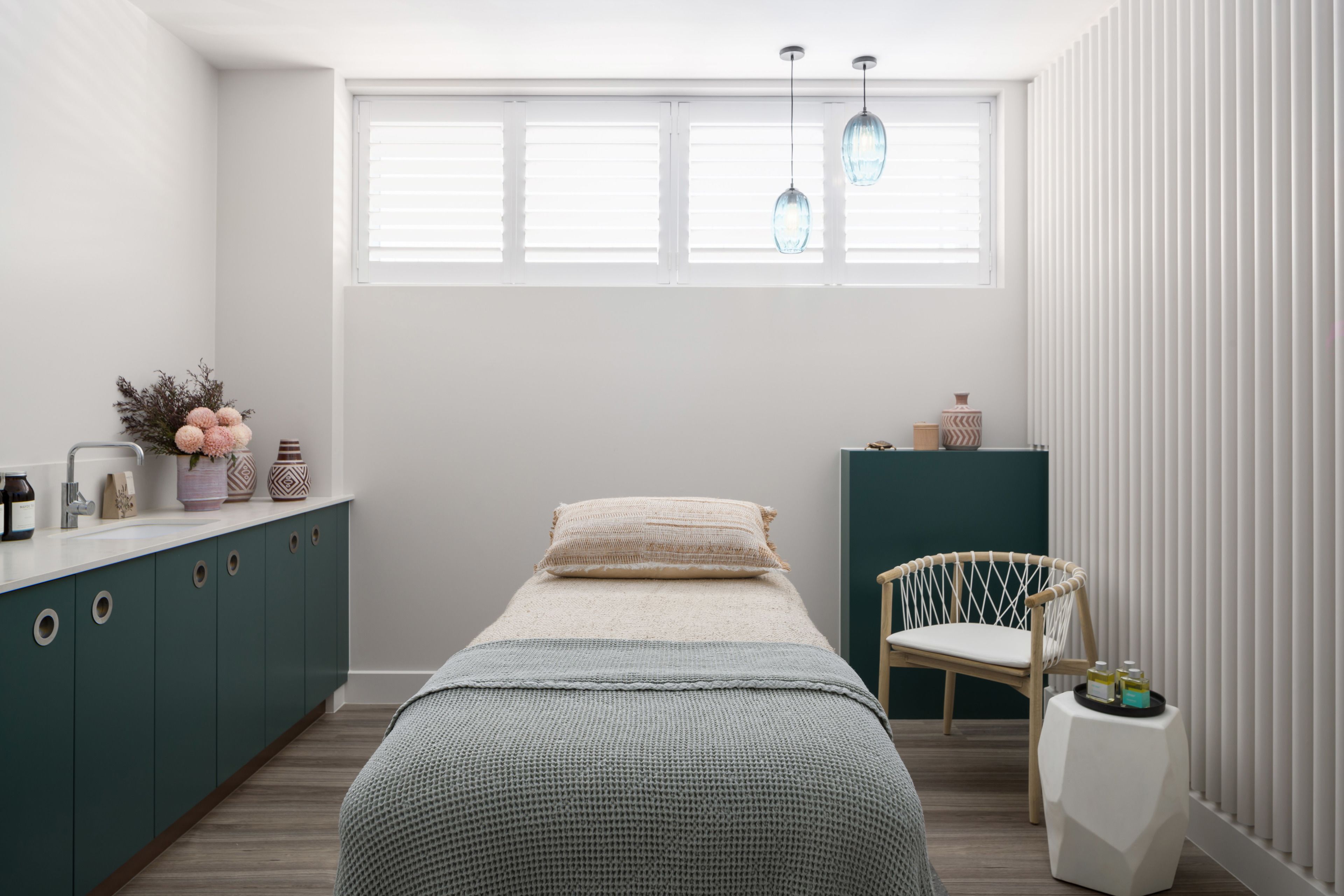 Quarto minimalista com cama, cadeira, cômoda e janela com persianas.