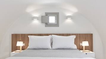 Quarto com cabeceira de madeira, duas mesas de cabeceira com abajures, uma janela e luminária na parede.