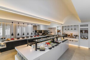 Uma disposição moderna de buffet, com vários pontos de comida, vitrines de vidro e iluminação pendente.
