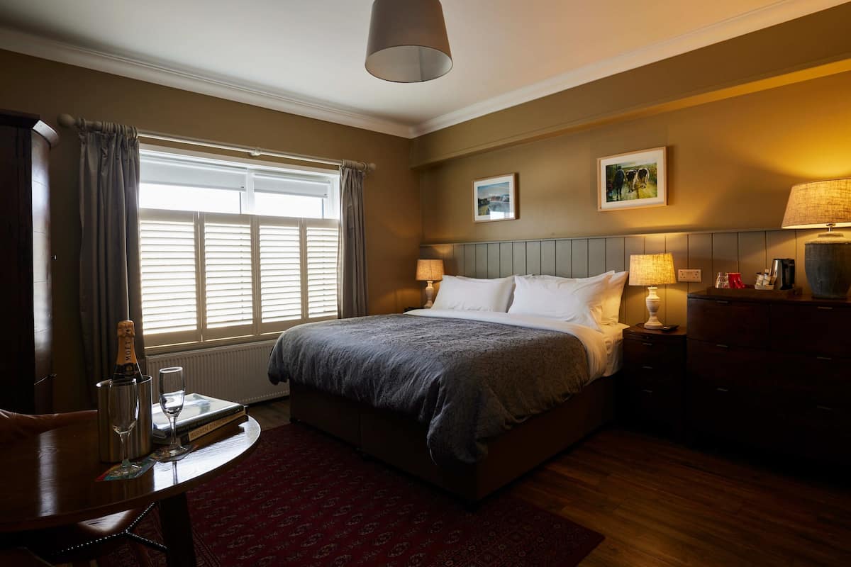 Quarto de hotel com cama, abajures, mesa de cabeceira, penteadeira de madeira, janela com cortinas e tapete vermelho.