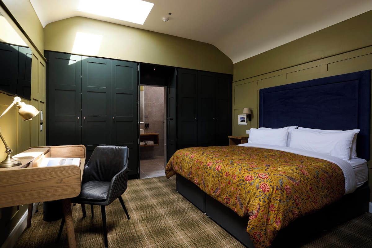 Quarto de hotel com cama, escrivaninha, cadeira e guarda-roupa.