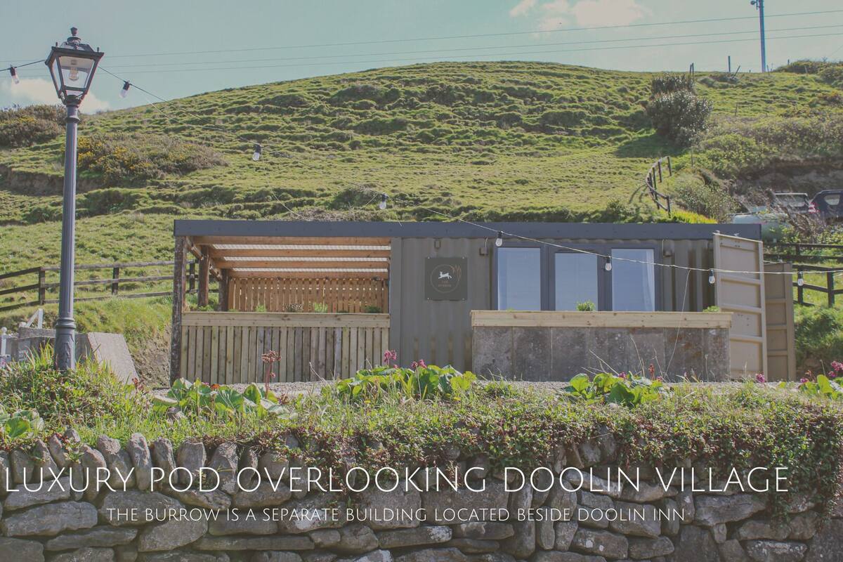 Uma acomodação de luxo com vista para a Vila de Doolin, com uma construção separada que possui um deck de madeira e paredes de pedra.