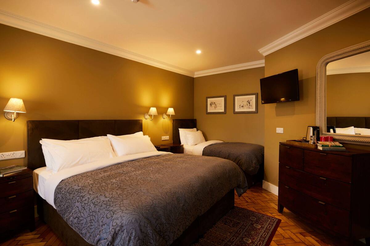 Quarto de hotel com duas camas, cômoda, televisão e luminárias fixadas na parede.