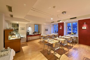 Uma área de refeições com mesas, cadeiras, um balcão de buffet e janelas com vista.