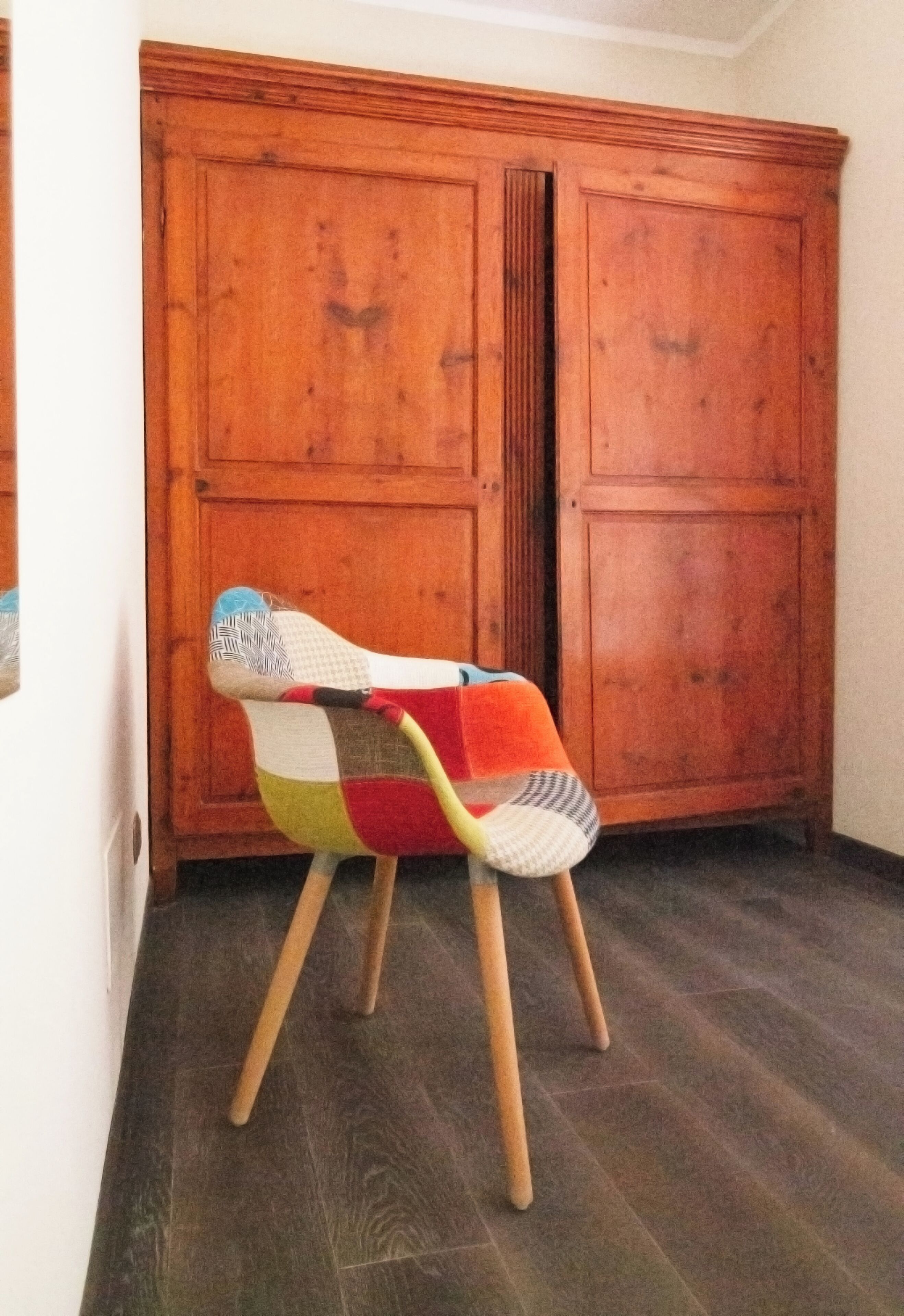 Uma cadeira com um design colorido e de patchwork em um quarto com armários de madeira e piso de madeira escura.