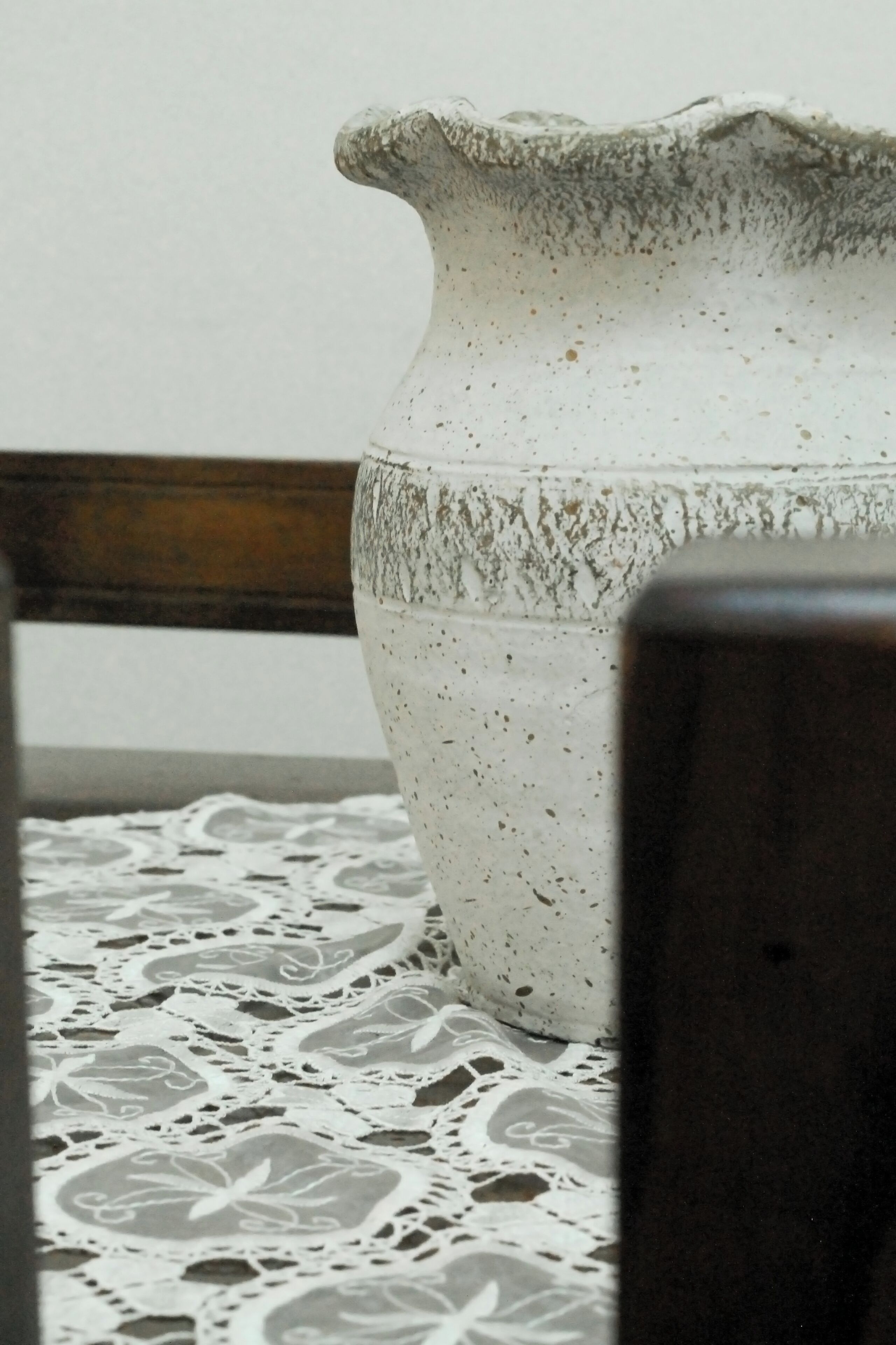 Uma panela de cerâmica branca com superfície texturizada, colocada sobre uma toalha de renda.