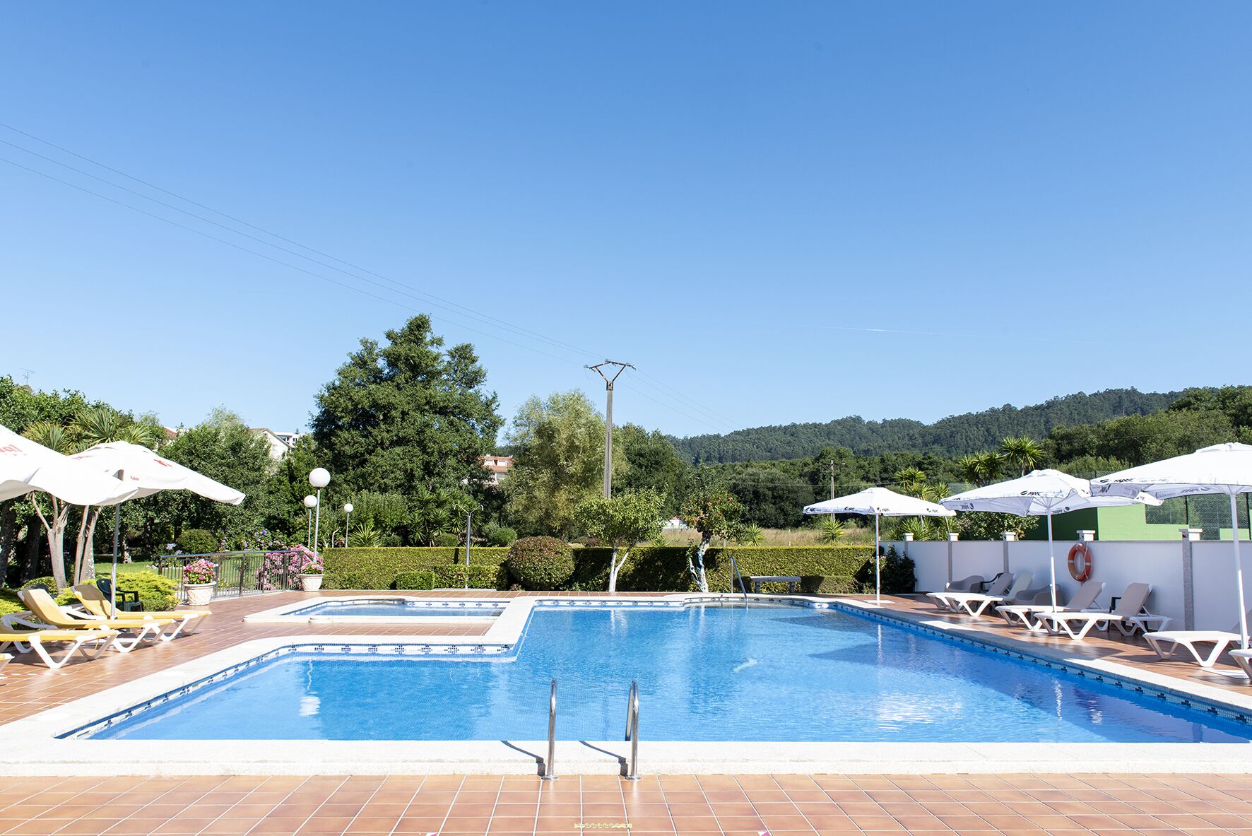 Piscina retangular com duas plataformas de mergulho, rodeada por espreguiçadeiras e guarda-sóis.