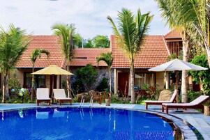 Uma área de piscina com espreguiçadeiras, piscina e um edifício com telhado de telhas vermelhas.
