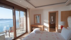Quarto de hotel com uma cama grande, uma escrivaninha de madeira, banheiro e varanda com vista para o mar.