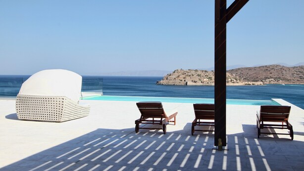 Área de piscina com espreguiçadeiras e um espaço coberto para sentar, com vista para o mar.
