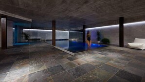 Piscina interior moderna com chão de pedra, rodeada por paredes e pilares, e um banco de um lado.