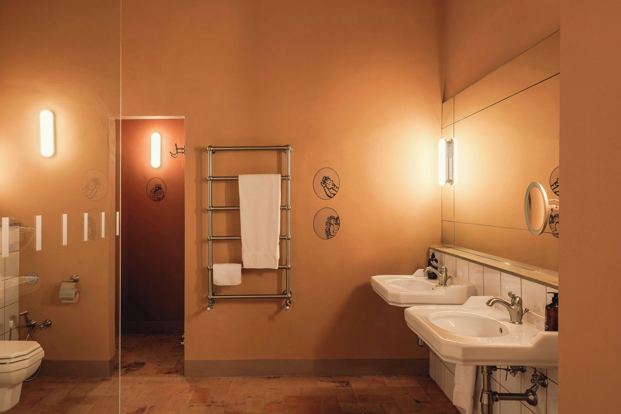 Casa de banho com duas pias, um porta-toalhas, um espelho e uma sanita.