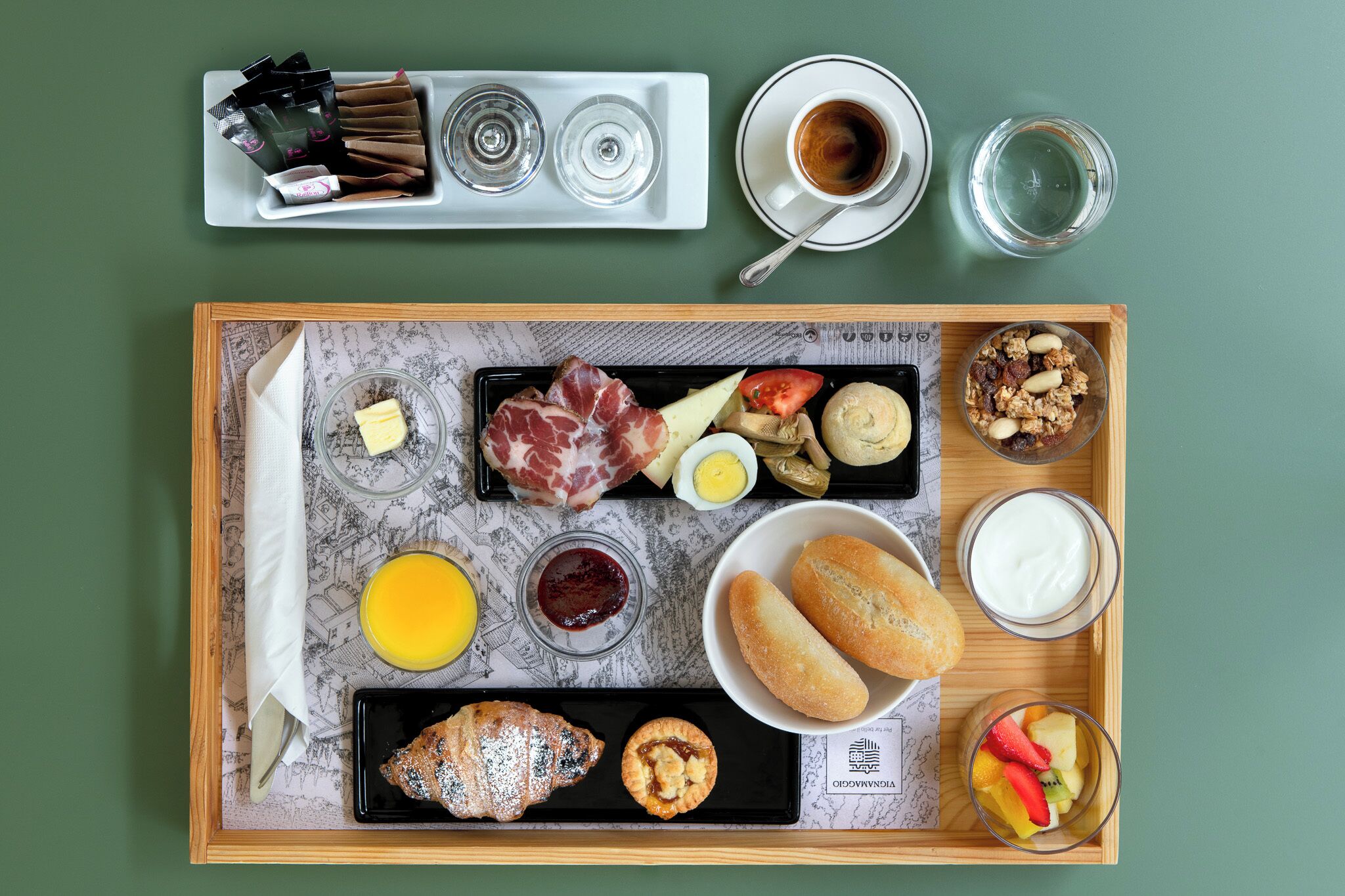 Bandeja de café da manhã com croissants, presunto, queijo, ovos e frutas.