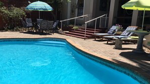 Uma piscina com borda azulejada, rodeada por espreguiçadeiras e guarda-sóis.